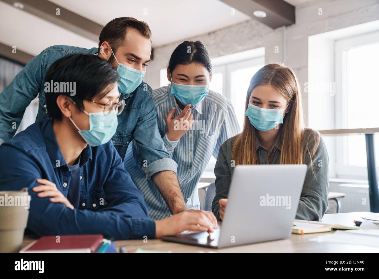 Photo of multinational pleased students in medical masks studying with ...