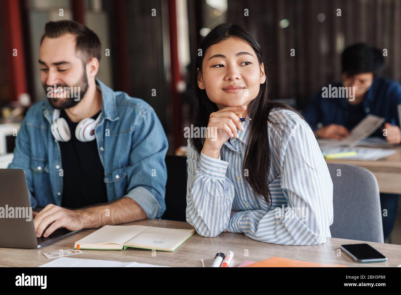 Photo of multinational young students using laptop and smiling while ...
