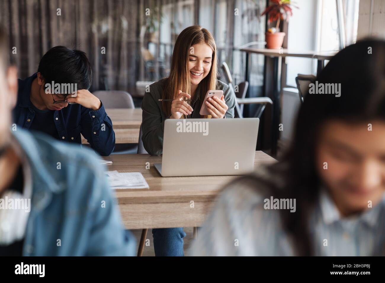 Photo of multinational young students using laptop and smartphone while ...
