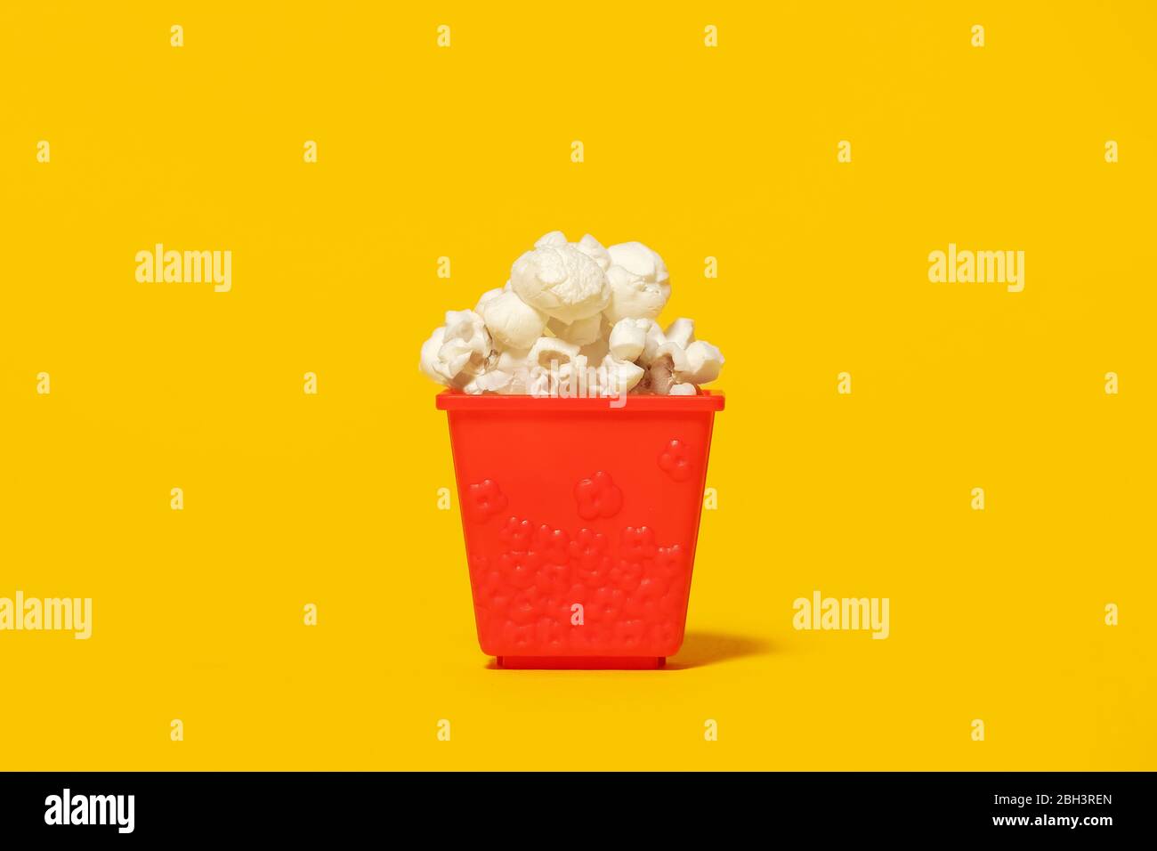 Red popcorn box carton full of popped popcorn on a yellow background ...