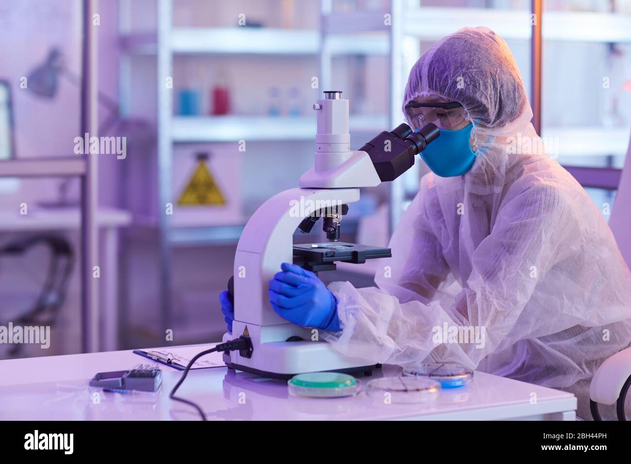 Medical worker wearing protective clothing examining samples through ...