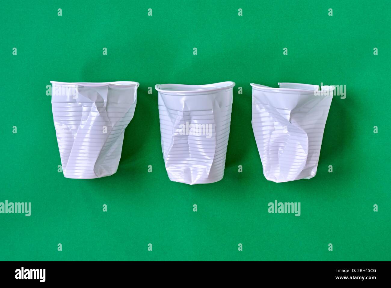Three smashed white plastic coffee cups on a green background with copy ...