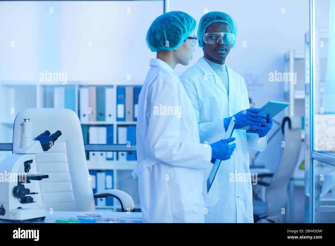 Two scientists in white coats discussing scientific experiment together ...