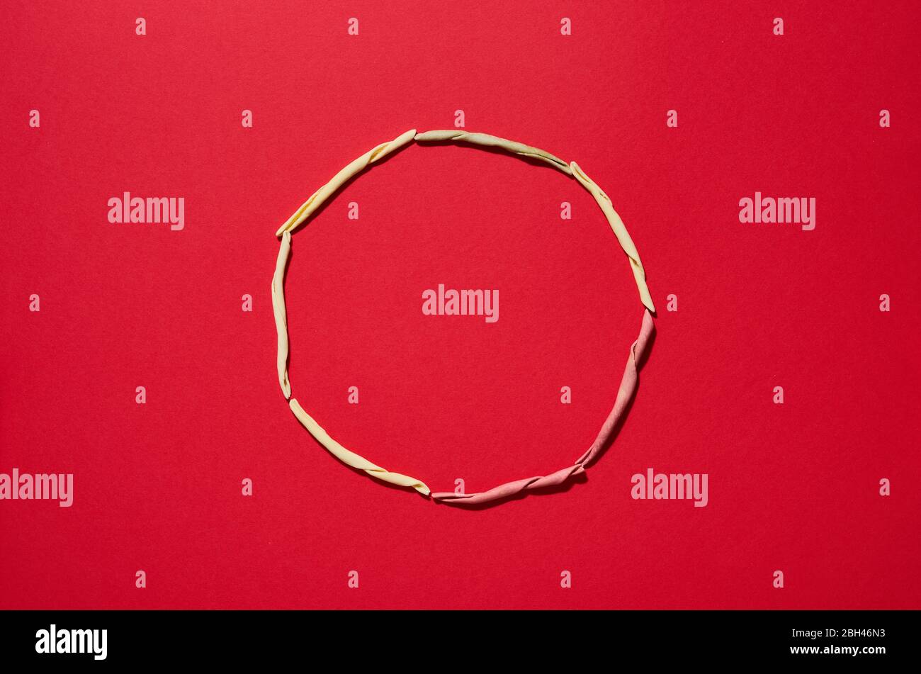 Italian fileja pasta in circle shape on the red background. Flat lay ...