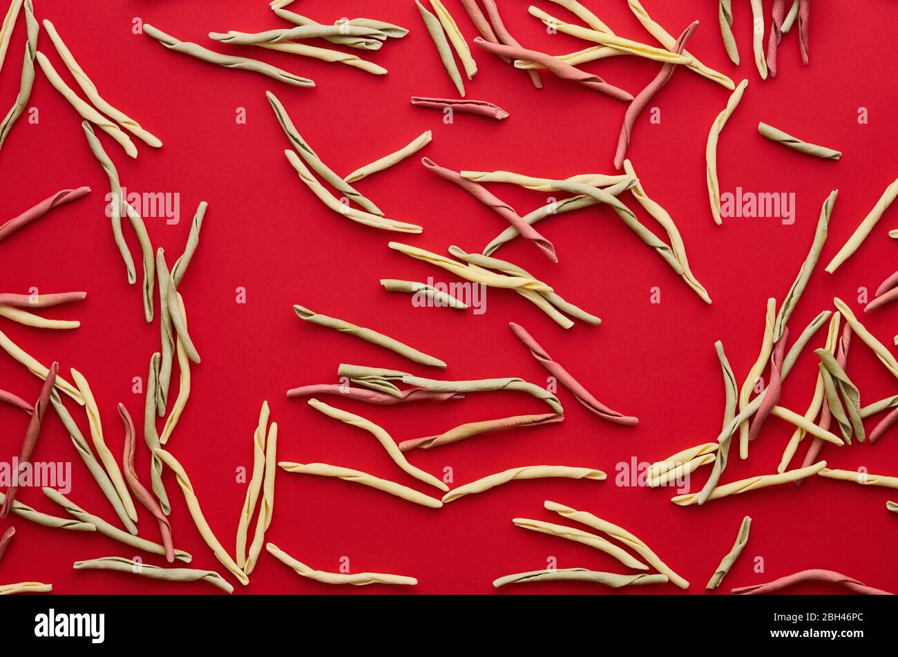 Italian fileja pasta of various colors and shapes on a red background ...