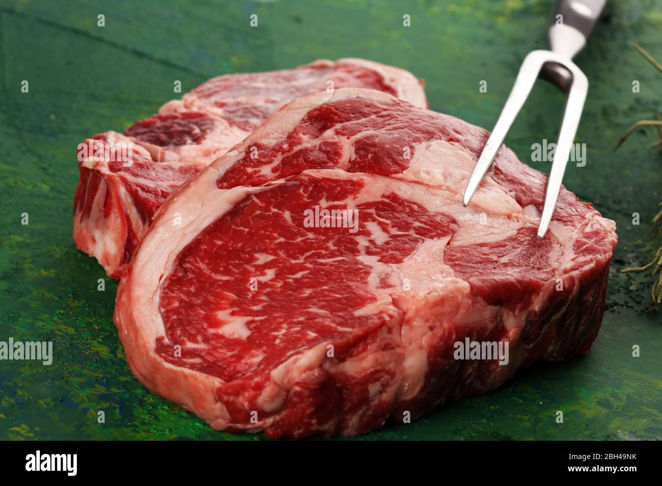 Two fresh raw rib-eye steak with rosmary in a rustic style background ...