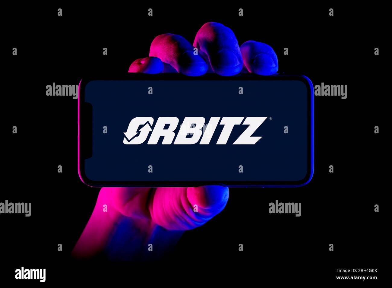 A smartphone displaying the Orbitz logo is held by a hand shot on a ...
