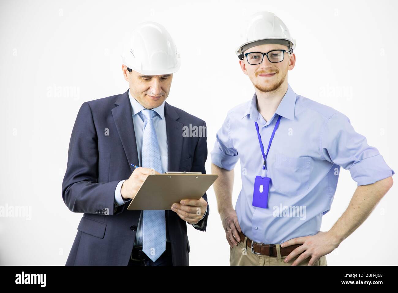 Two engineers different ages look at camera smiling, making notes on ...