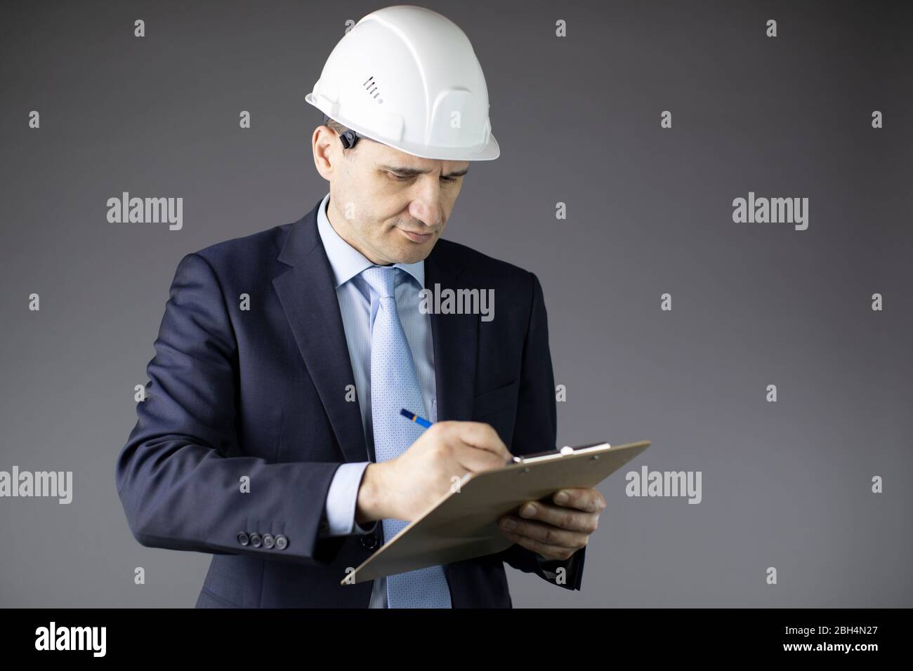 thoughtful handsome builder oilman wearing white helmet writes on ...
