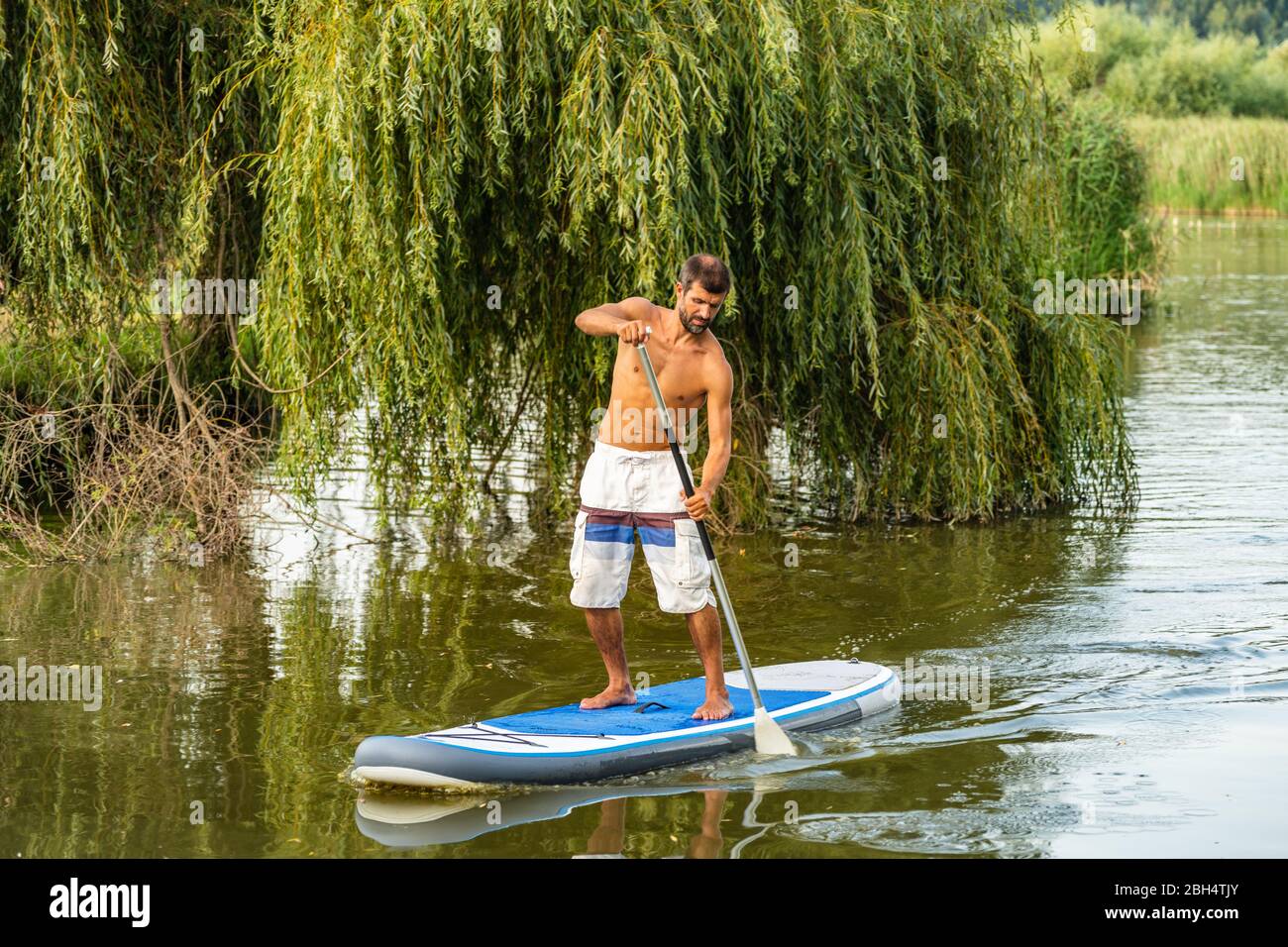 Man stand up paddleboarding on lake. Young man doing watersport on lake ...