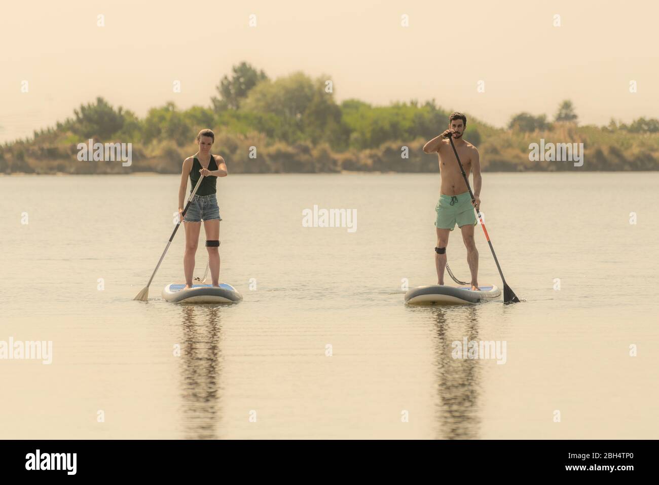 Man and woman stand up paddleboarding on lake. Young couple are doing ...