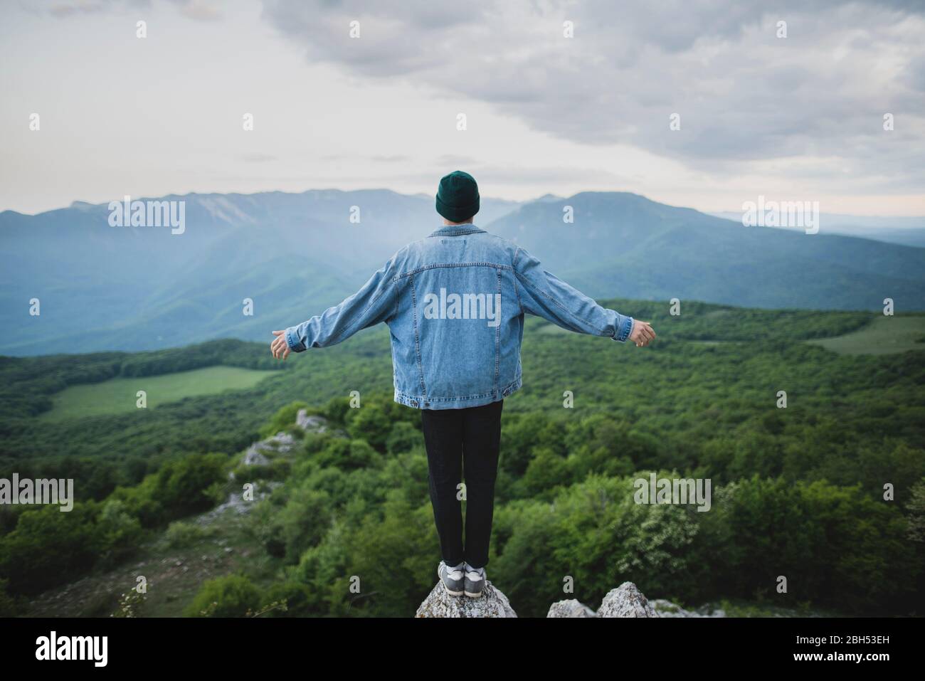 Man standing on cliff by mountain and forest Stock Photo - Alamy