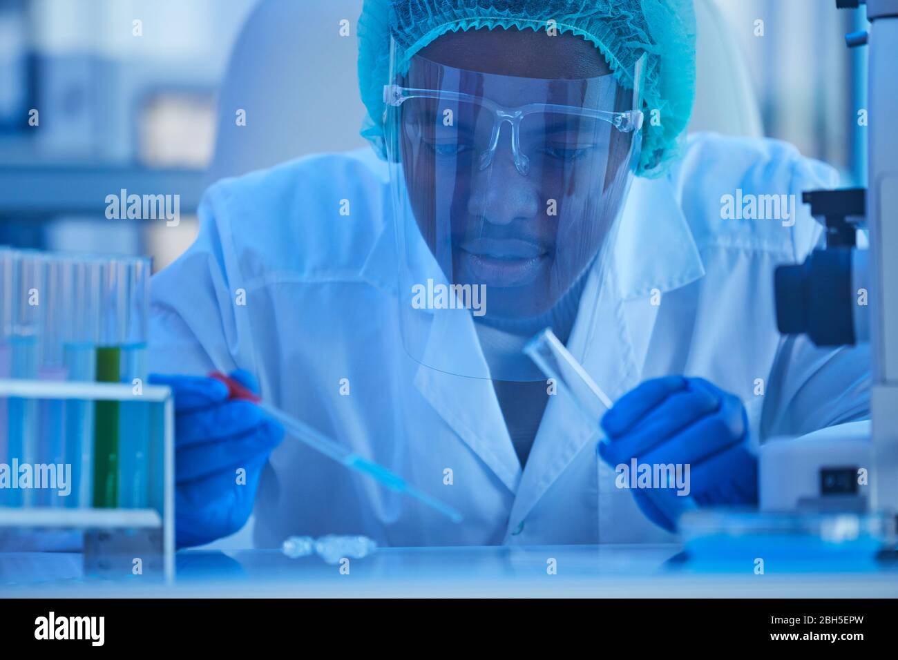 African doctor in protective mask working with samples from tube at ...