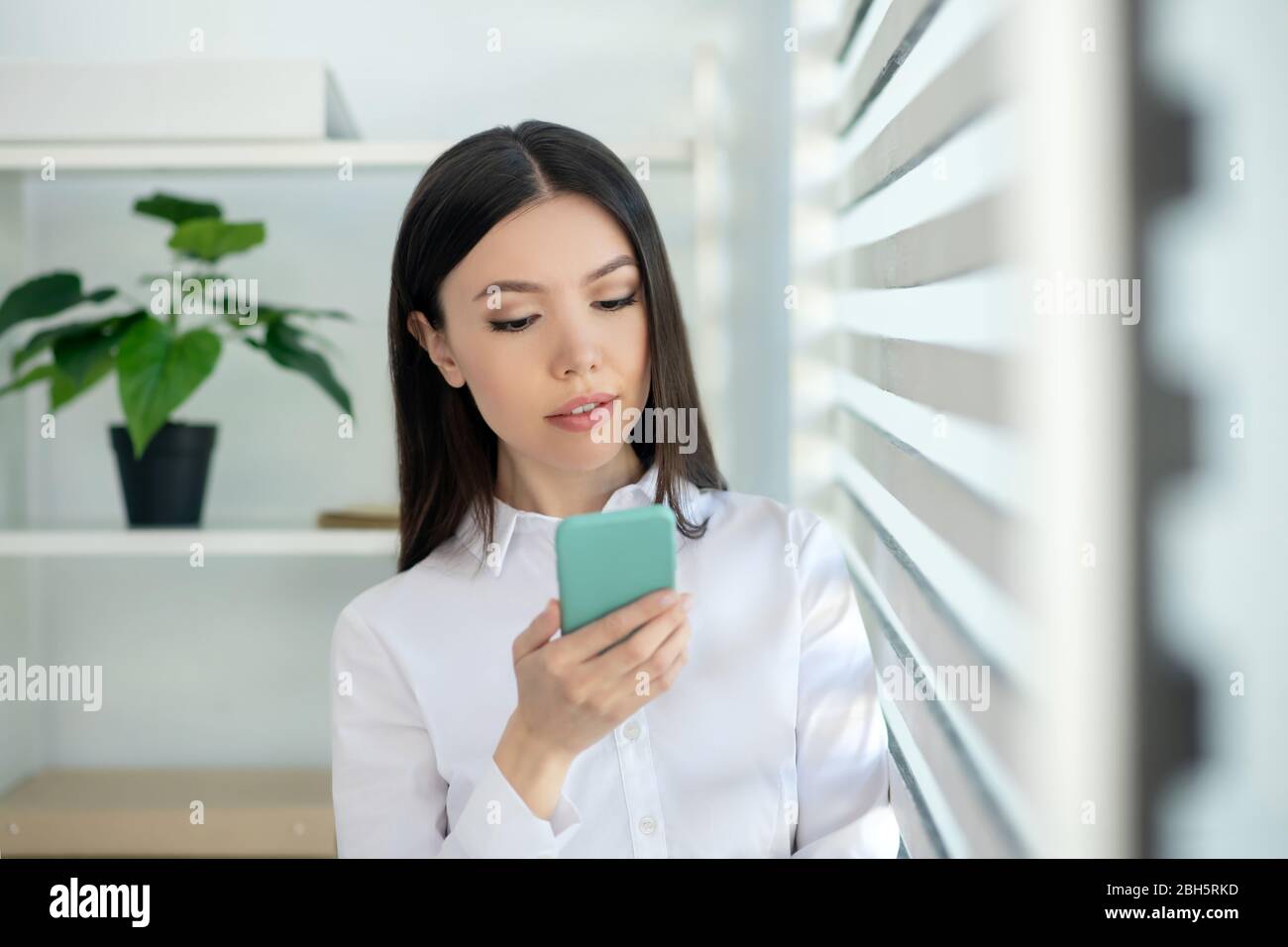 At work. Young brunette female standing at the window, checking her ...