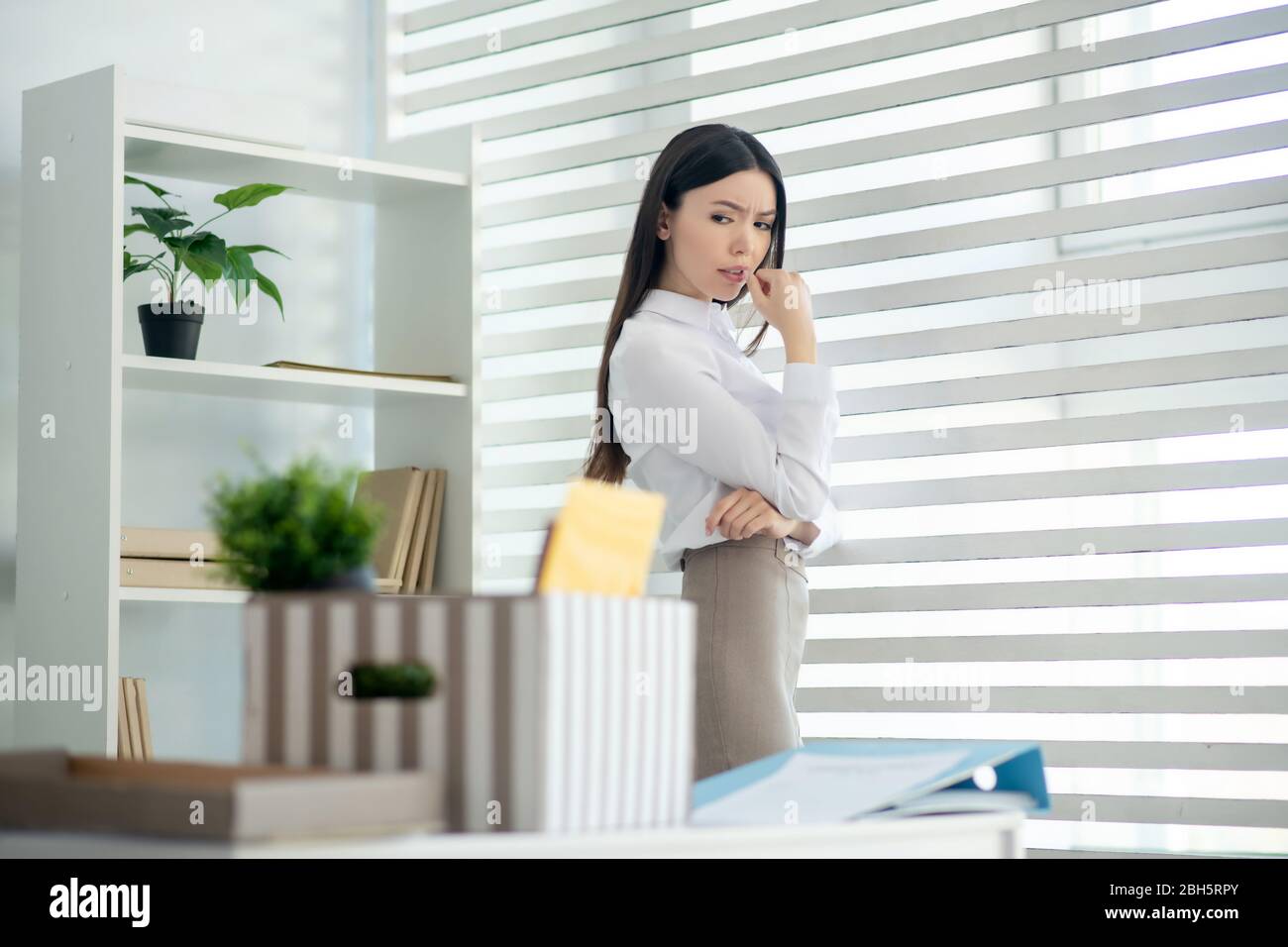 At home. Young brunette female standing at the window, looking at her ...