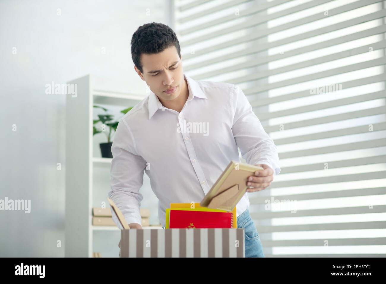 At work. Brunette male standing at his desk, gathering his personal ...