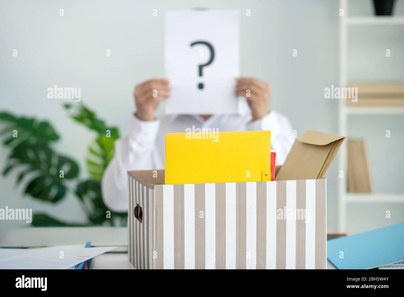 At work. Young male sitting at his desk, holding sign with question ...