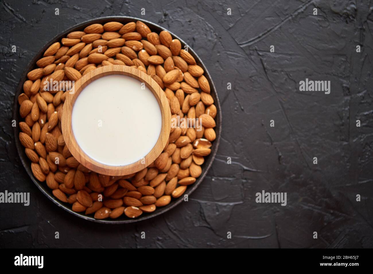 Composition of almonds seeds and milk, placed on black stone background ...