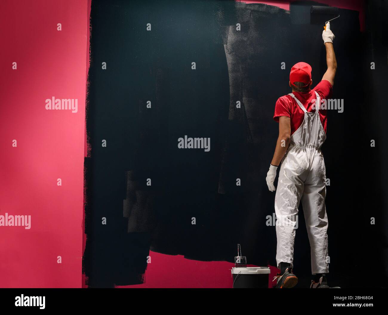 Man painting a wall. Painter in red overall painting wall in black ...