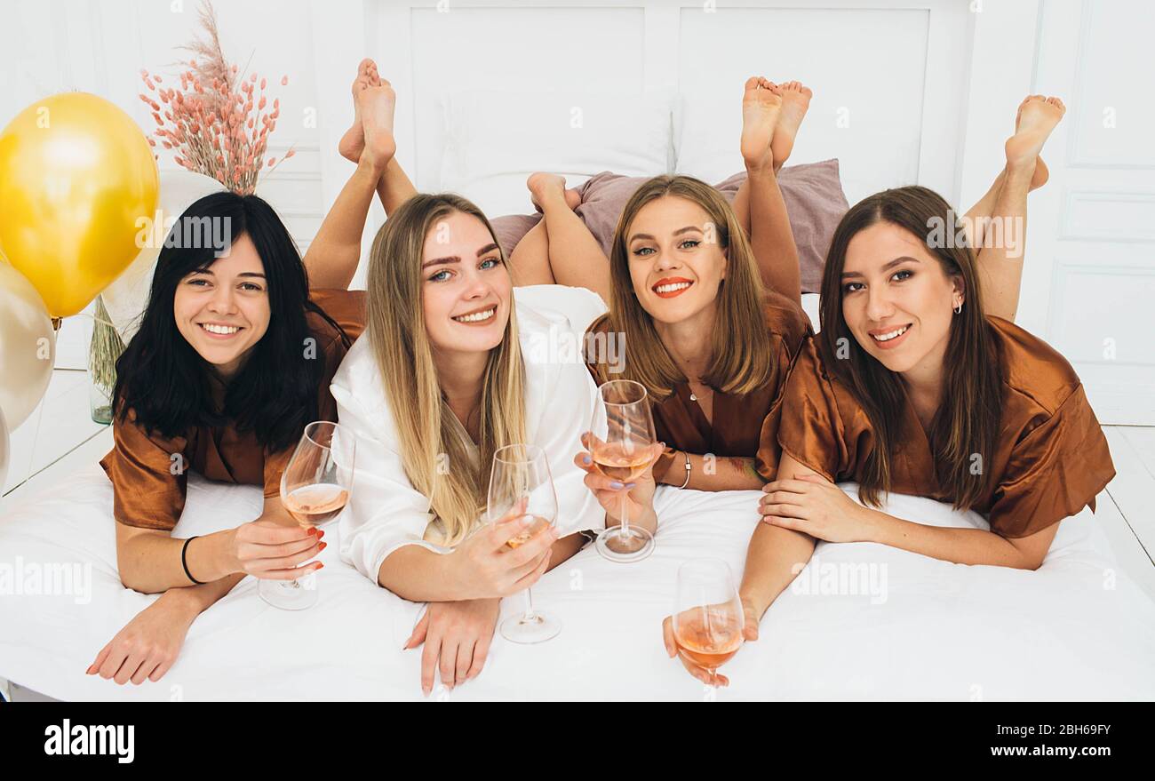 Four girlfriends with wine enjoying pajamas party at home. Celebrating ...