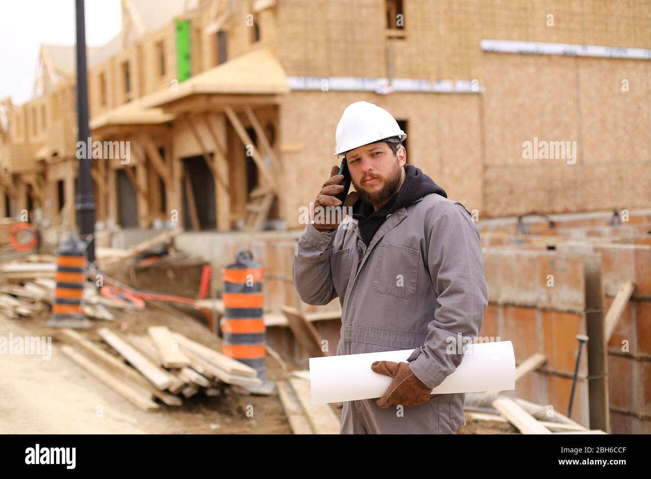 Builder talking by smartphone and holding drawing plan at construction ...