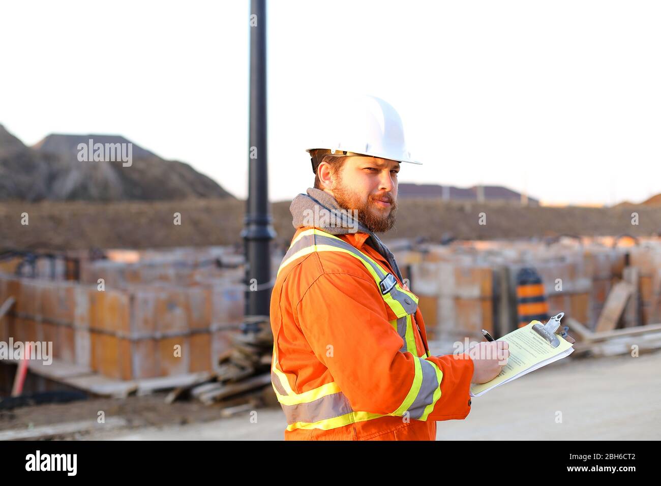 Caucasian inspector in orange workwear with blueprints on construction ...