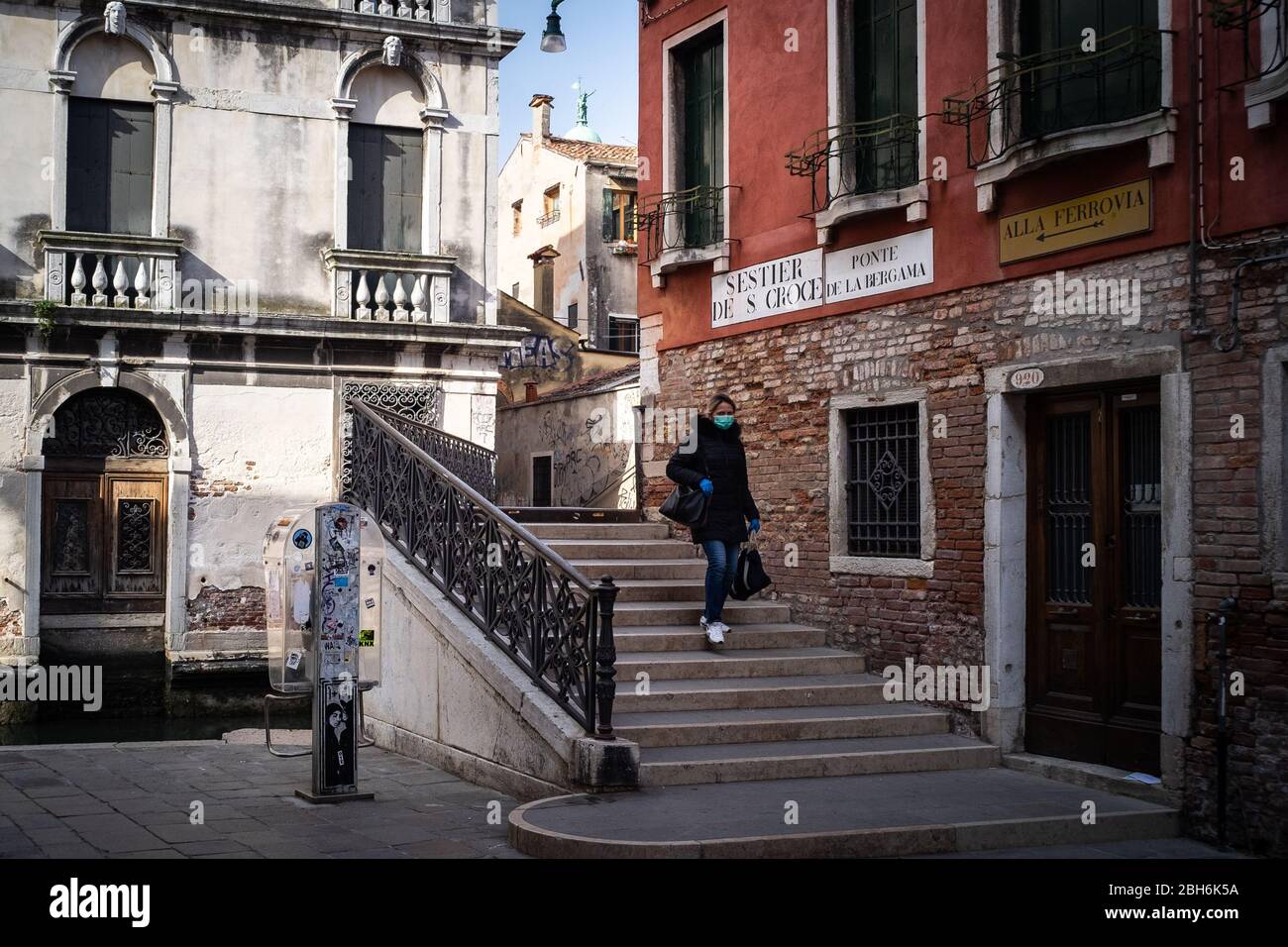 VENICE, ITALY - APRIL 2020: A woman wearing a protective mask crosses a ...