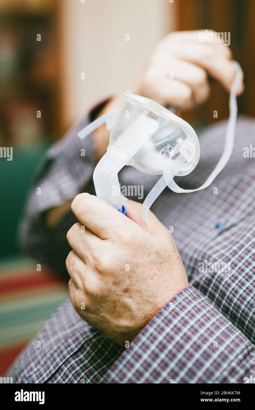 Senior man using medical equipment for inhalation with respiratory mask ...
