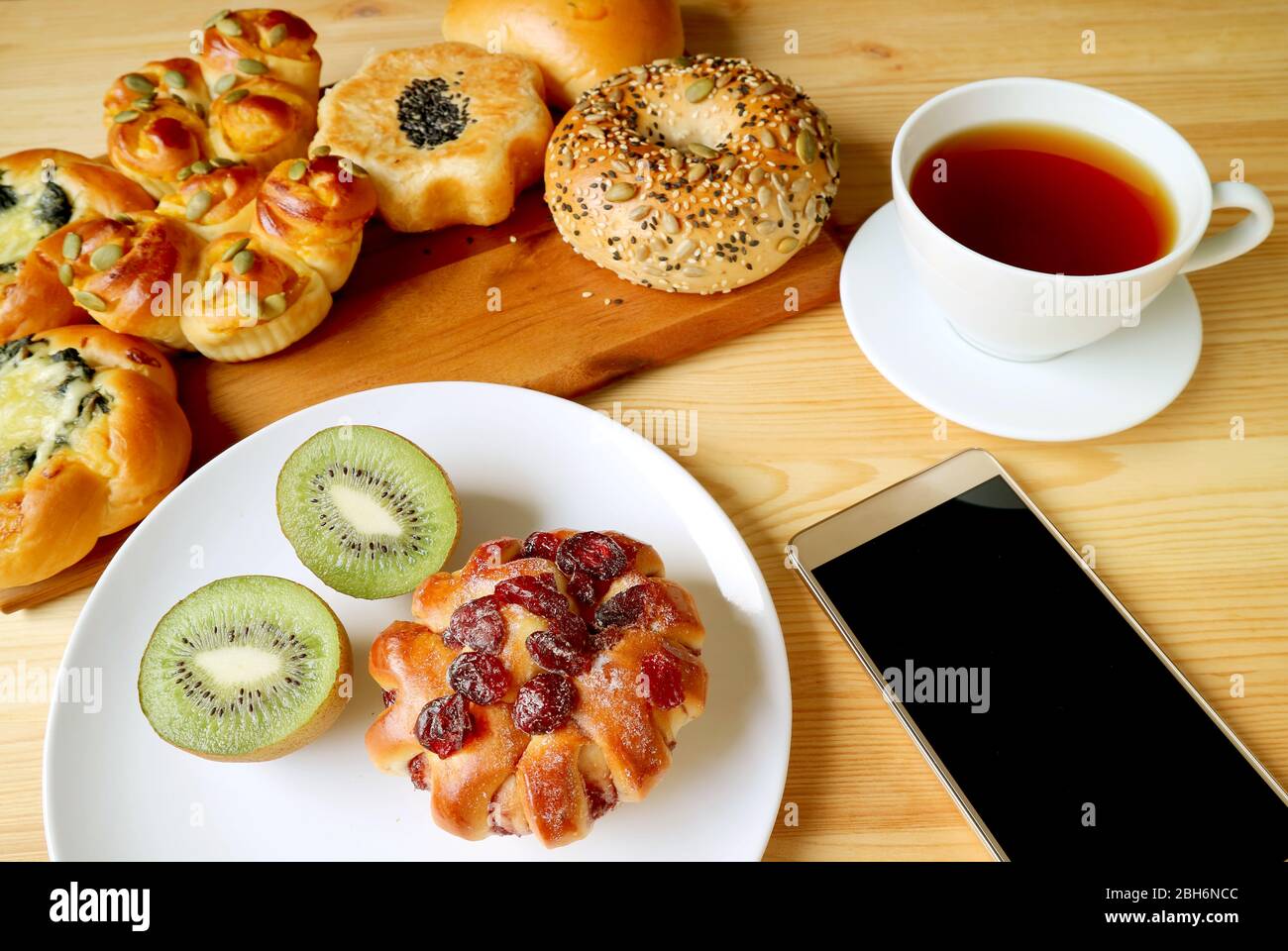 Assorted breads, kiwi fruit and hot tea for breakfast with mobile phone ...