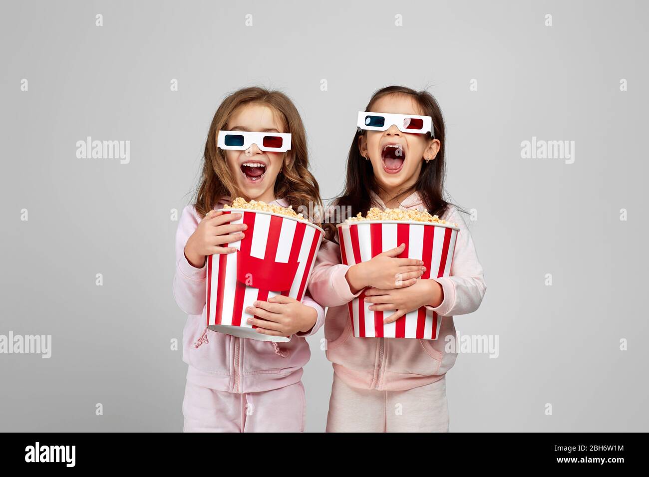 two beautiful surprised caucasian little girls in red-blue 3d glasses holding popcorn buckets ...