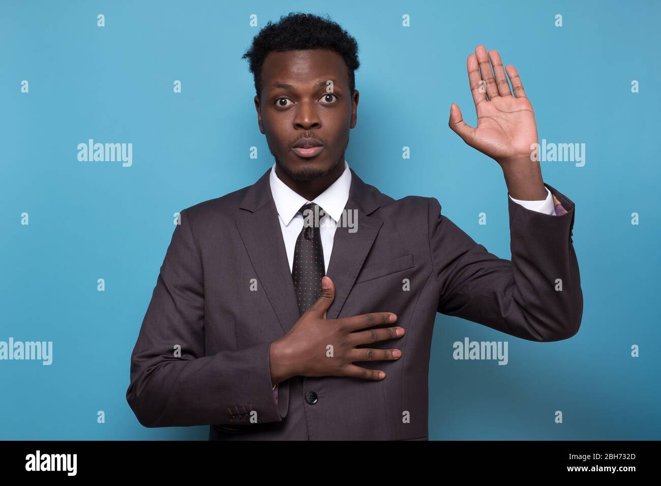 African american male in suit raising palm and holding hand on chest ...