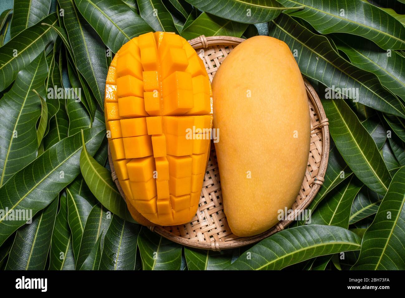 Mango, tropical fruit, in a bamboo wooden sieve basket on green leaf ...