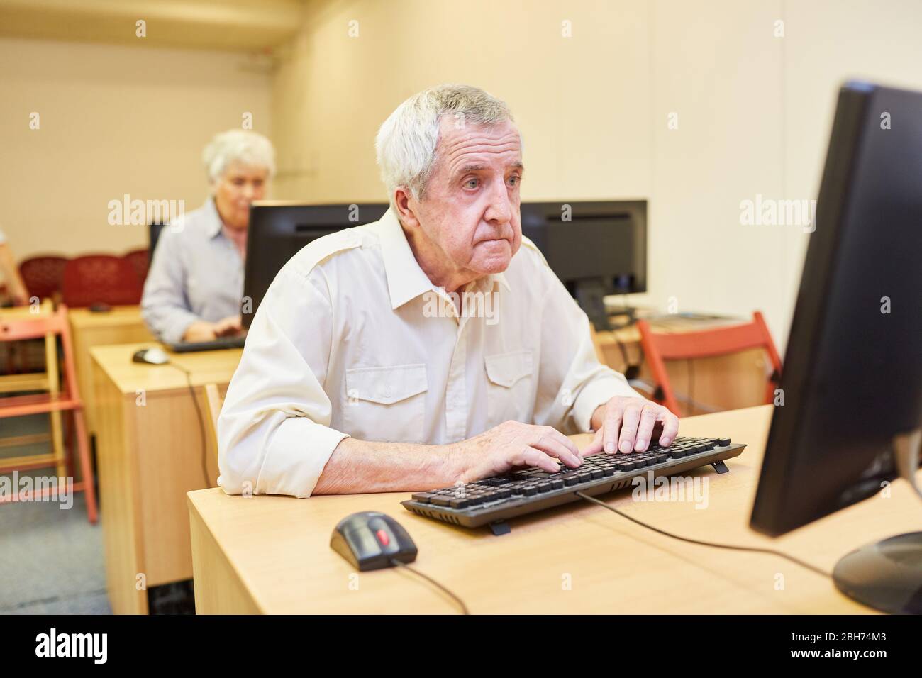 Senior man sitting on PC in a VHS computer course or retirement home ...
