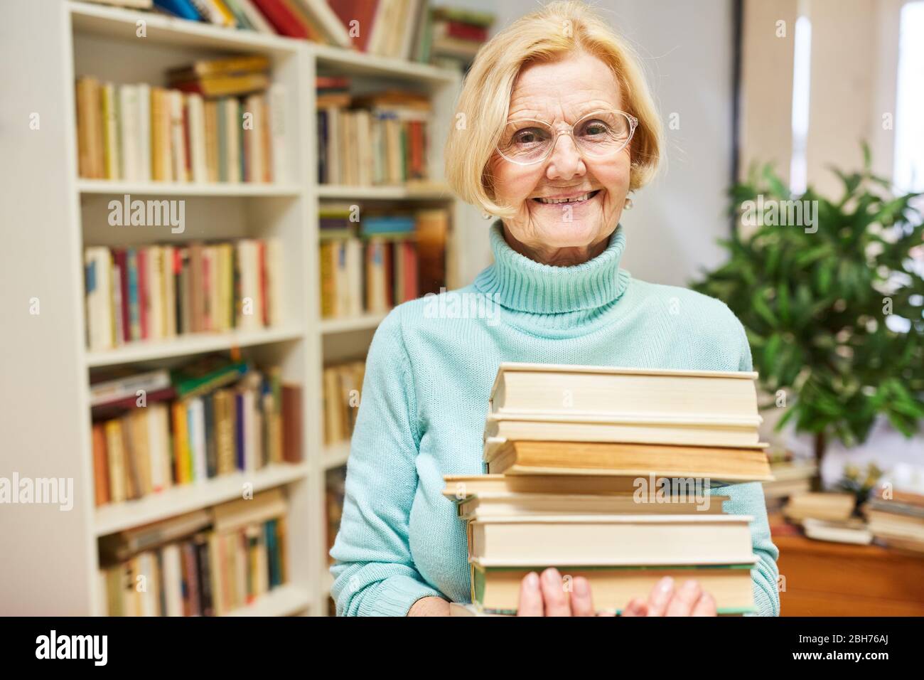 Happy senior woman as a librarian or antiquarian with a stack of books ...