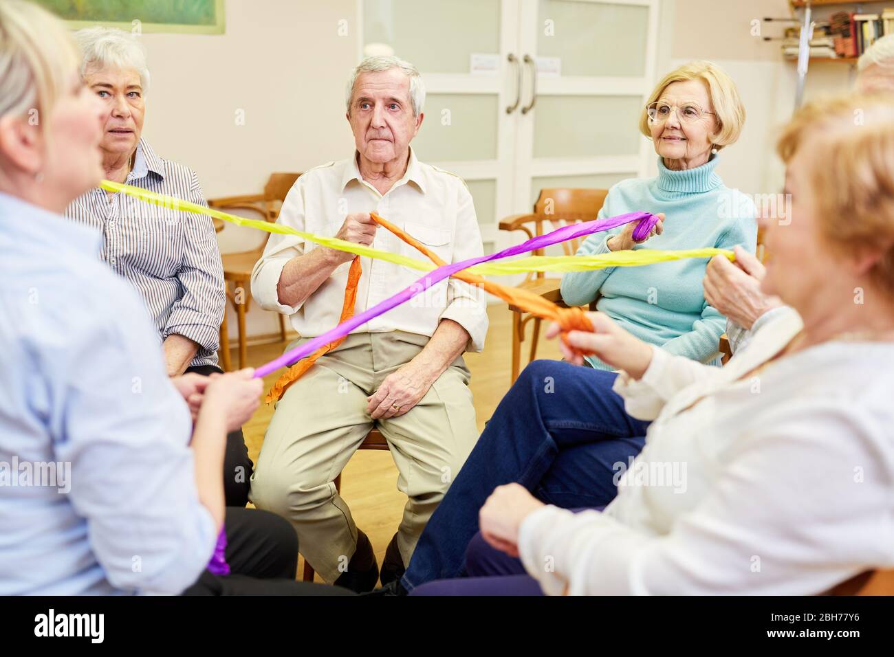 Therapist and seniors do exercise with colorful ribbons for cohesion ...