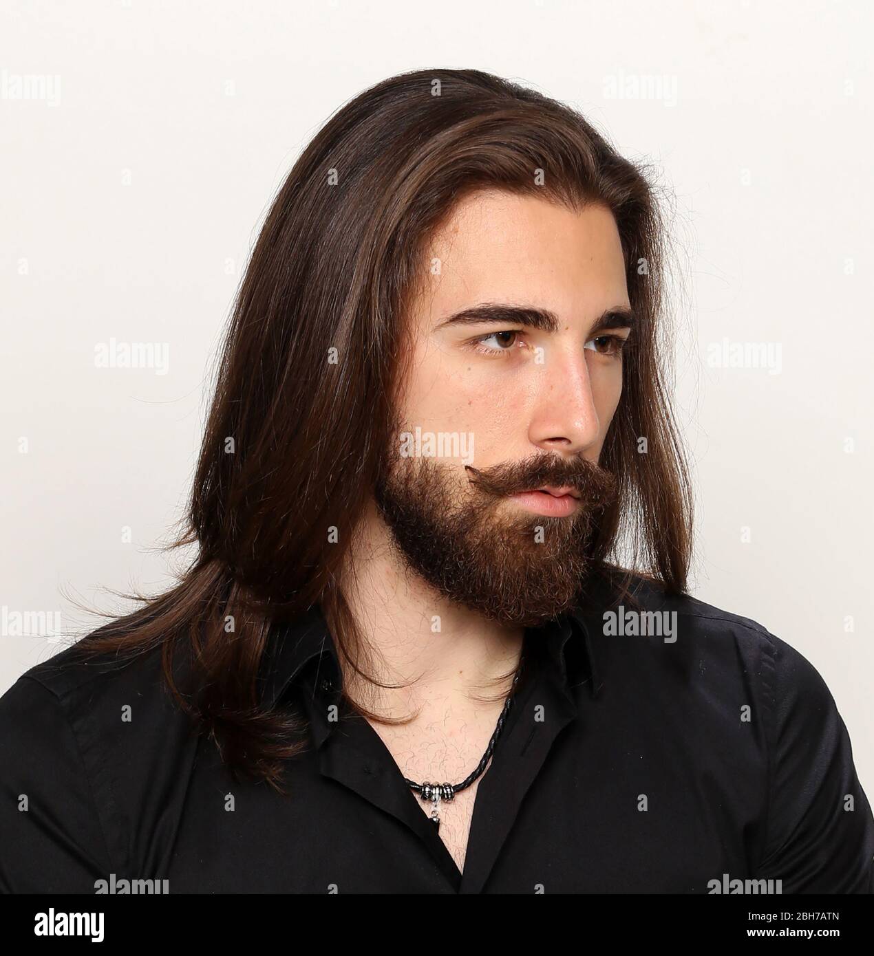 Young, fashionable male model with long hair and beard posing in studio ...