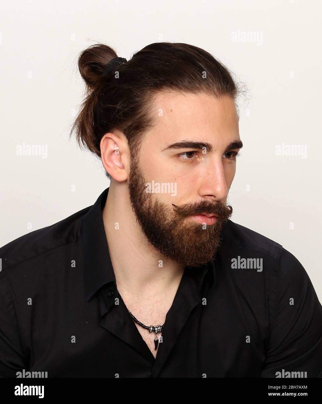 Young, fashionable male model with long hair and beard posing in studio ...