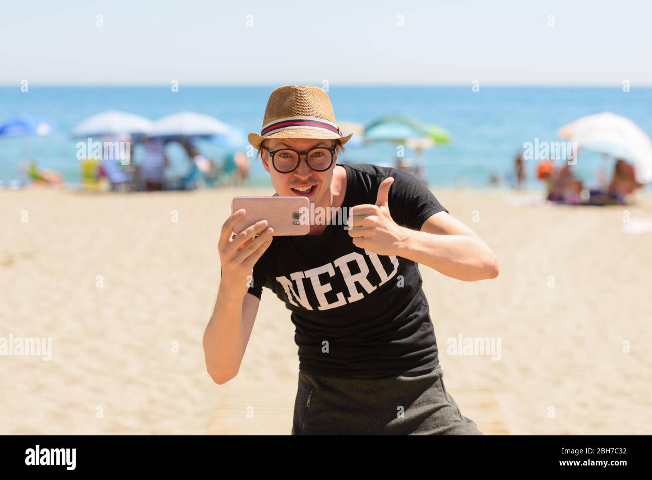 Happy young nerd tourist man taking picture with phone at the beach ...