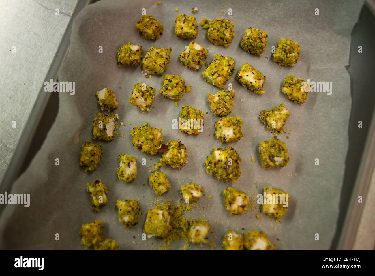 Cubes of feta cheese covered in ground pistachio nuts sit on a baking ...