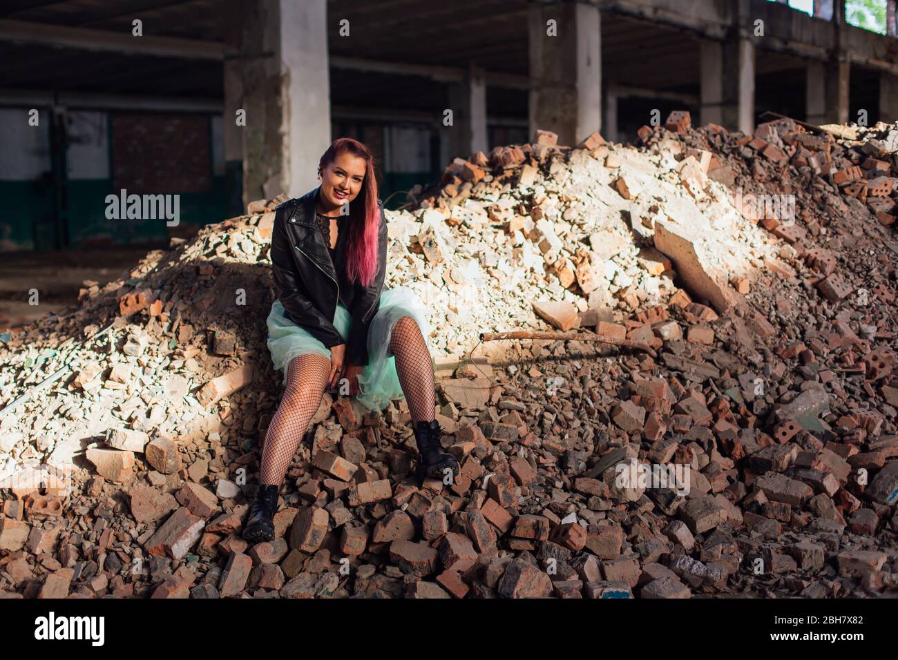 Young girl with pink hair sitting on bricks in a collapsed building ...