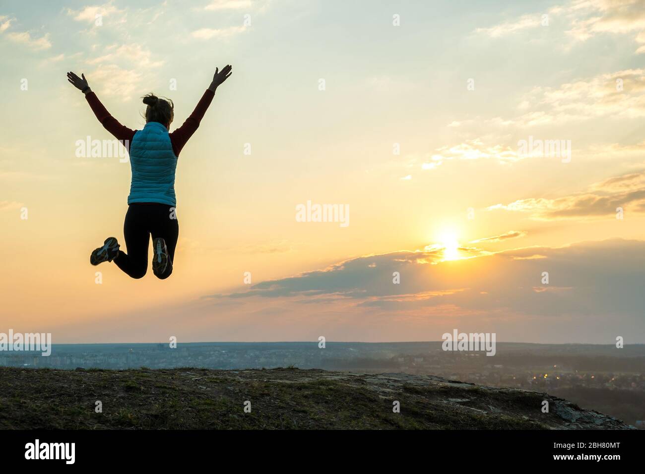 Silhouette of a woman hiker jumping alone on empty field at sunset in ...