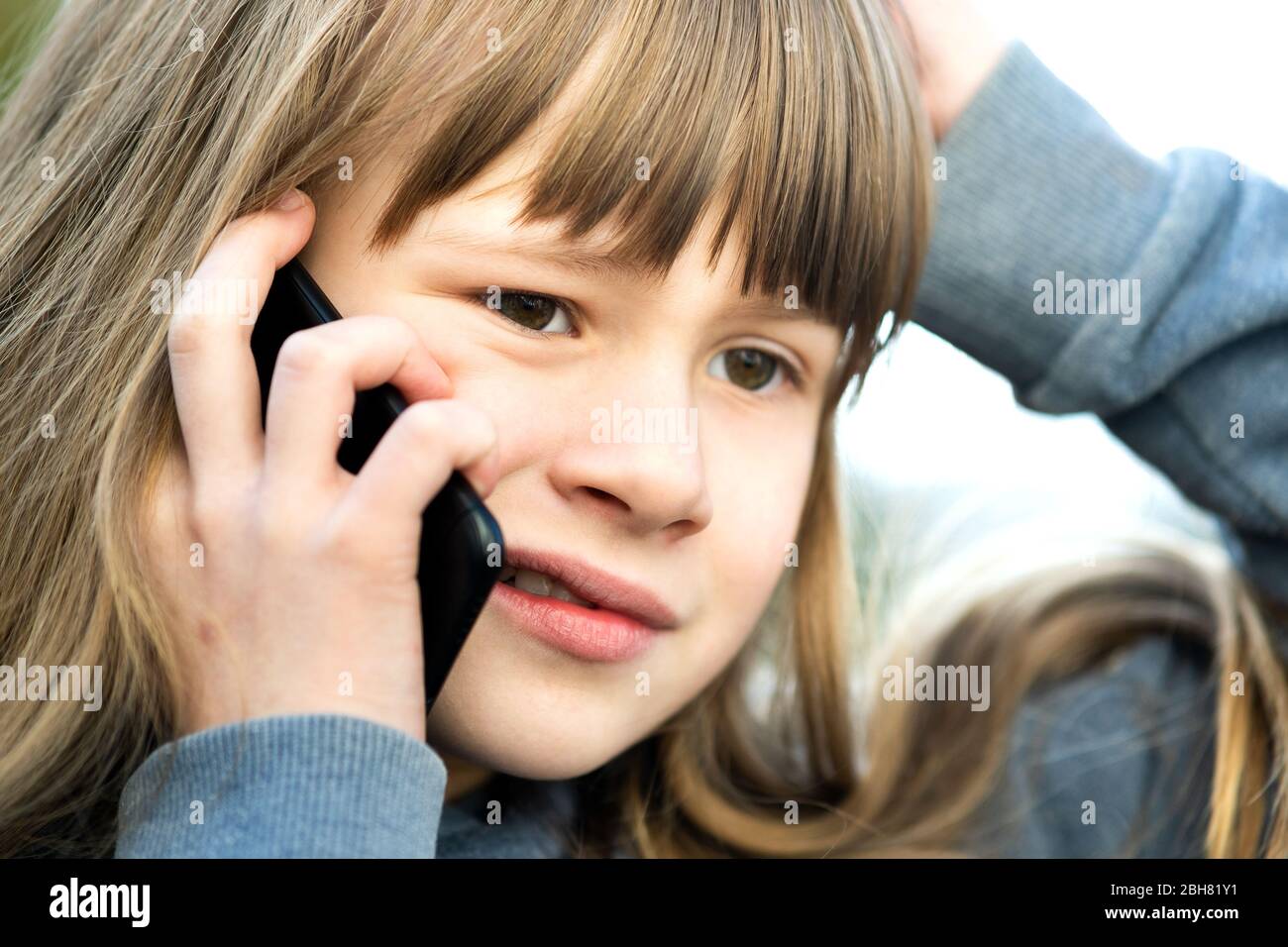 Portrait of stressed child girl with long hair talking on cell phone ...