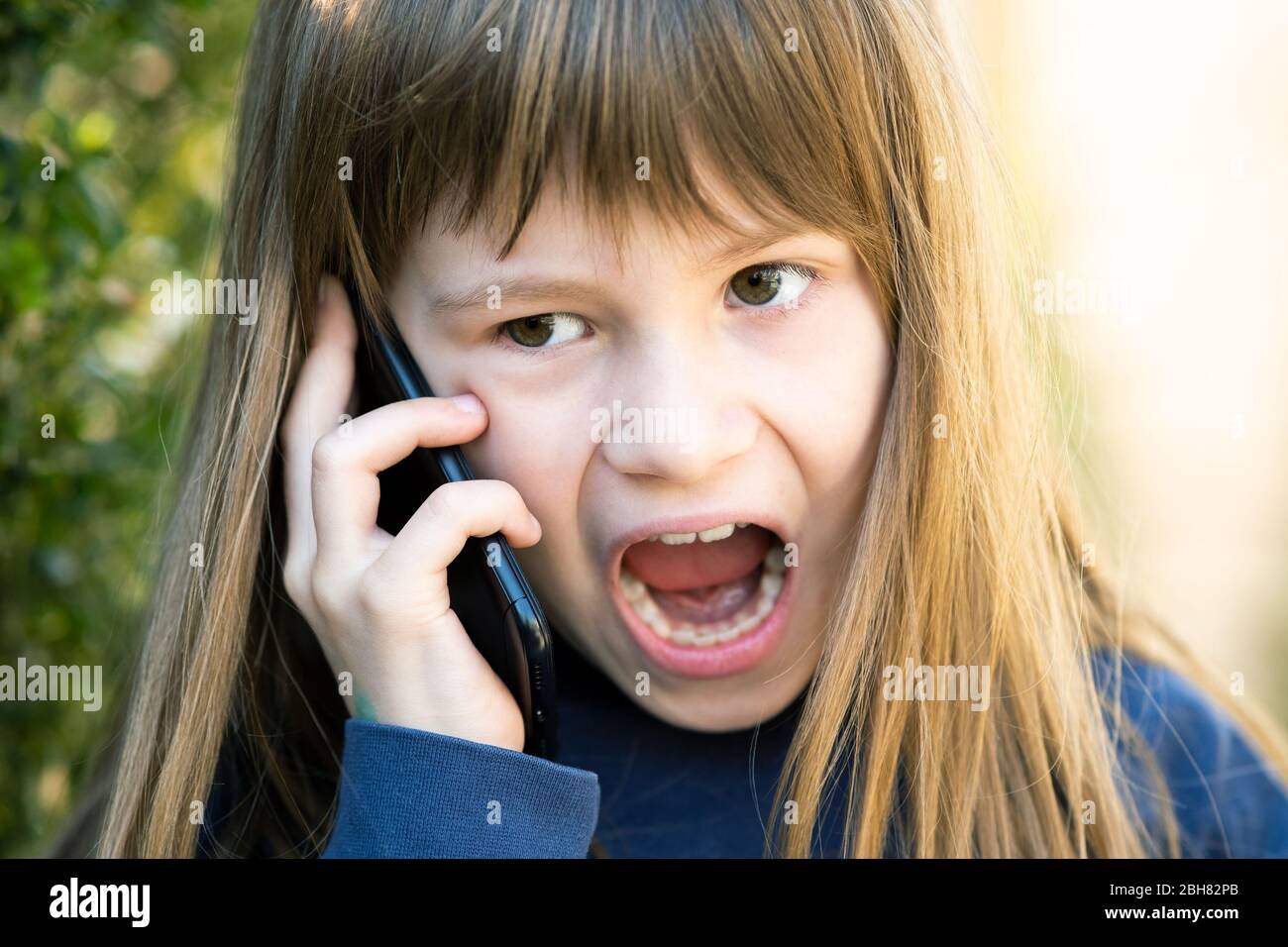 Portrait of angry child girl with long hair talking on cell phone ...