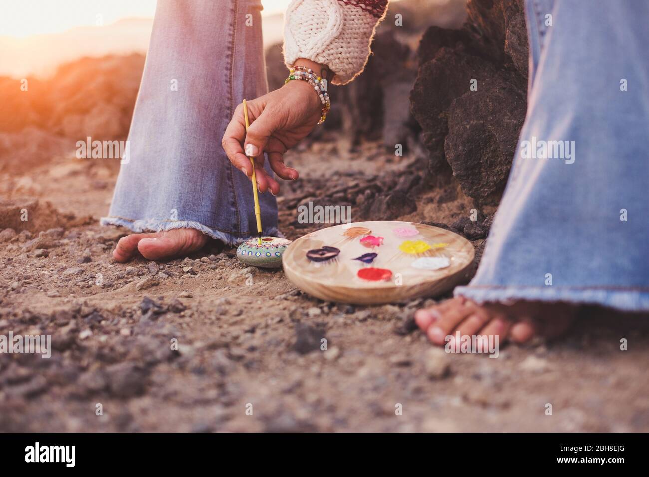 feet of woman barefoot on the ground while she paints a mandala on a ...