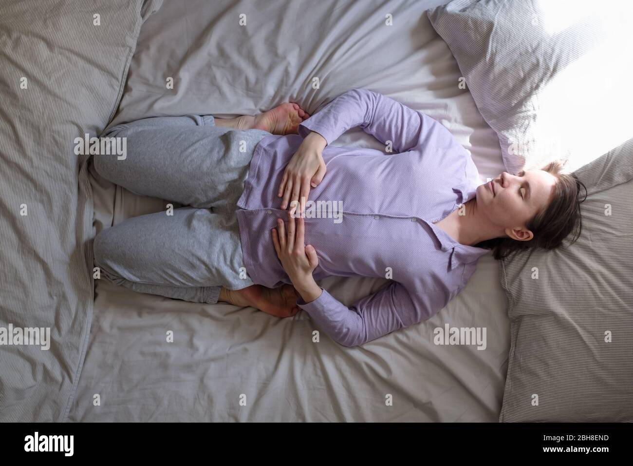 Caucasian young woman in reclining hero yoga Pose in bed at the morning ...