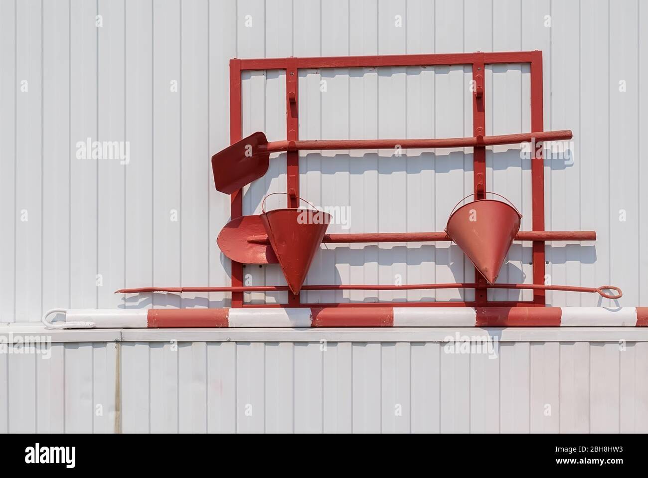 a red fire shield on a white metal wall with buckets, shovels, and ...