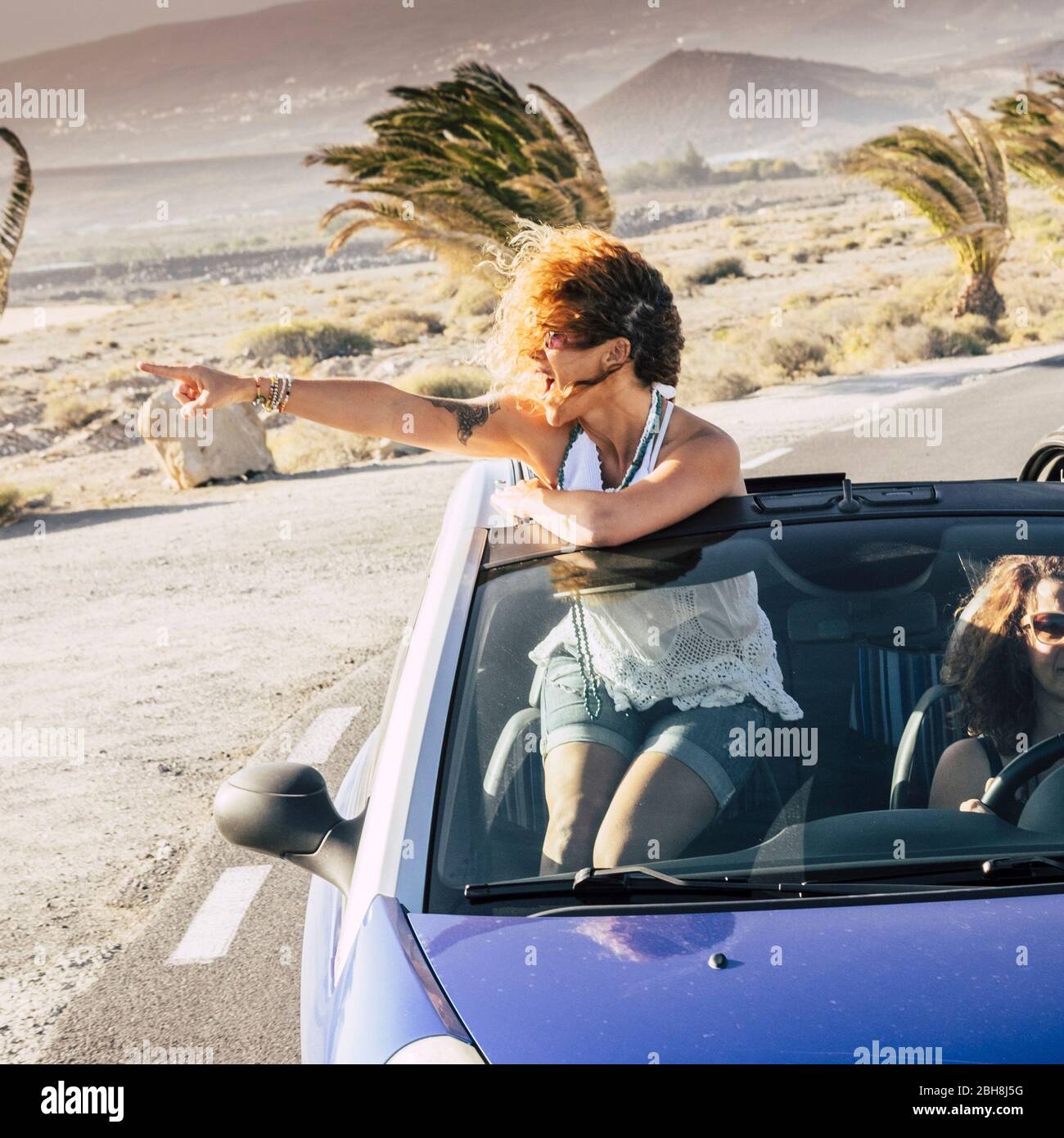 Happy blonde curly girl traveler on a convertible car standing and ...