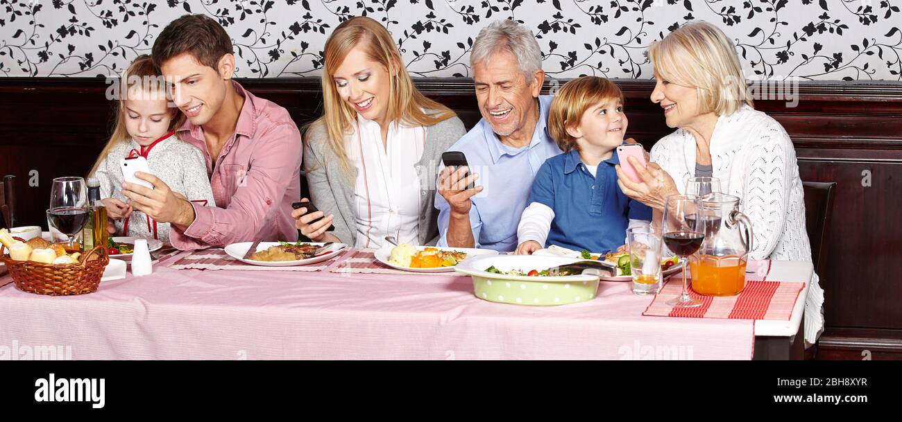 Large family eating together looks at different smartphones Stock Photo ...