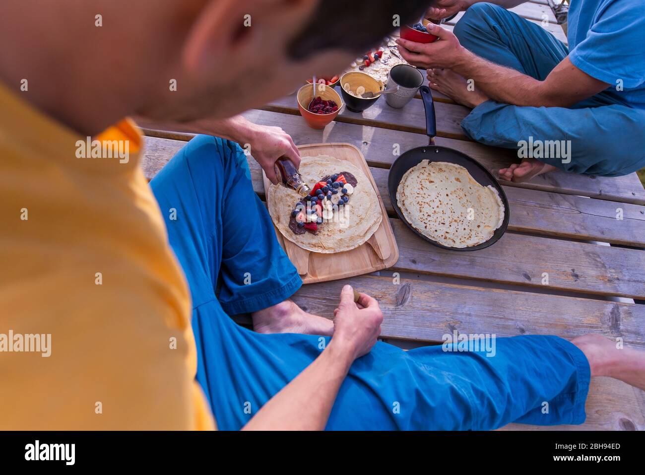man pouring maple syrup on sweet crepe sitting on wooden structure ...