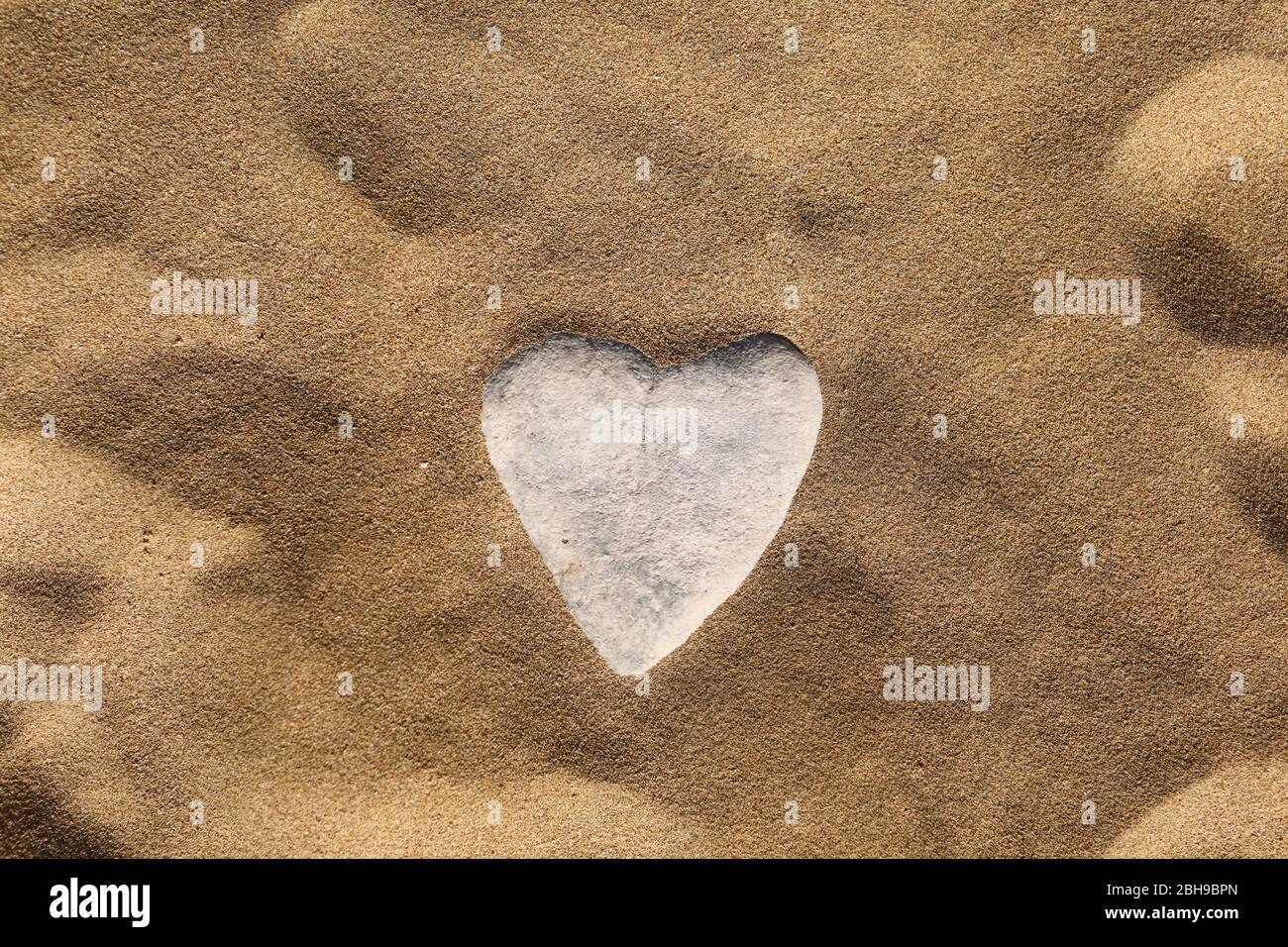Stone in the form of a heart on sand. Sea sand background, wallpaper ...